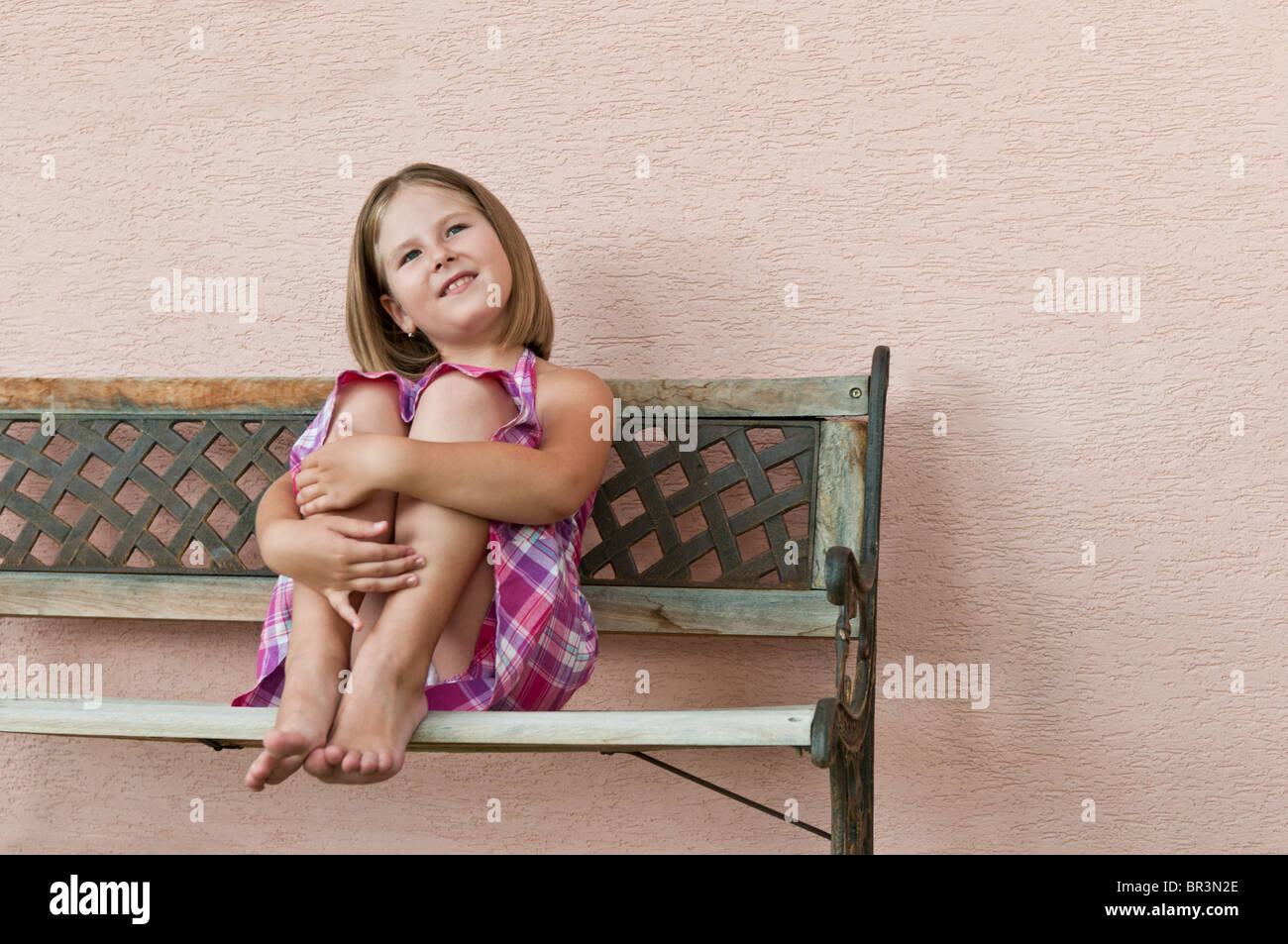 Portrait of cute smiling child sitting on bench and holding her legs ...
