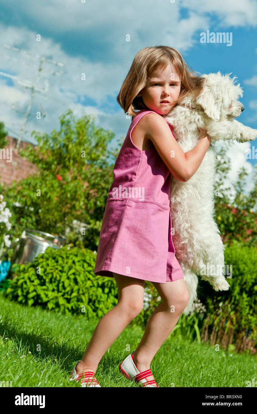 Small cute girl carrying her dog in garden behind family house Stock ...