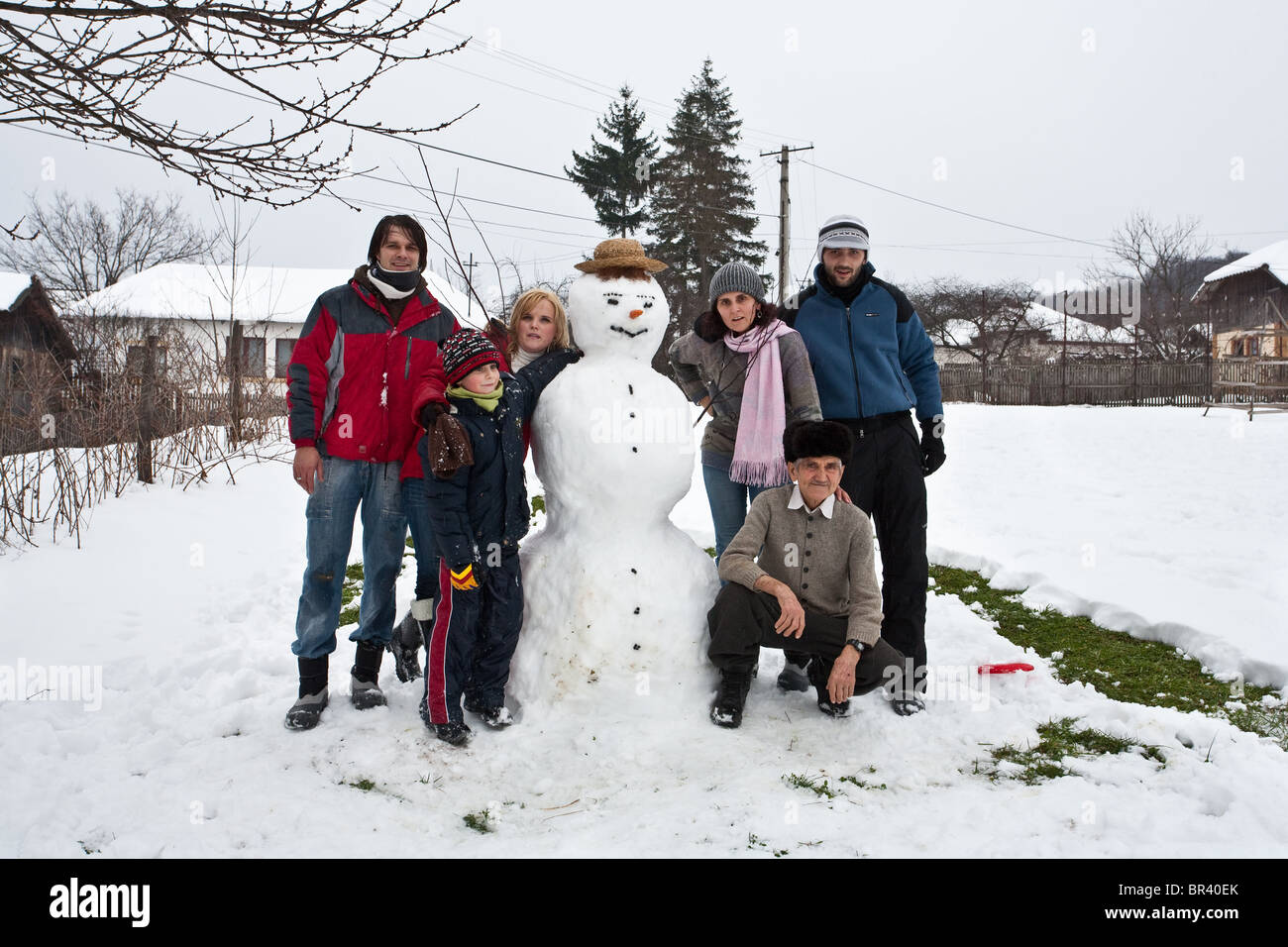 Multi generation family gathering happily together around a snowman, in ...