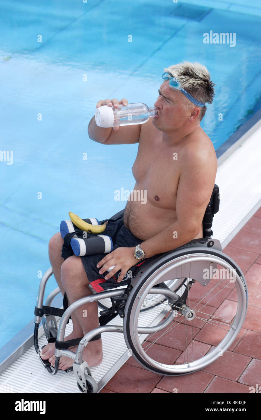 Young, handicapped man in a wheelchair at the edge of a swimming pool ...