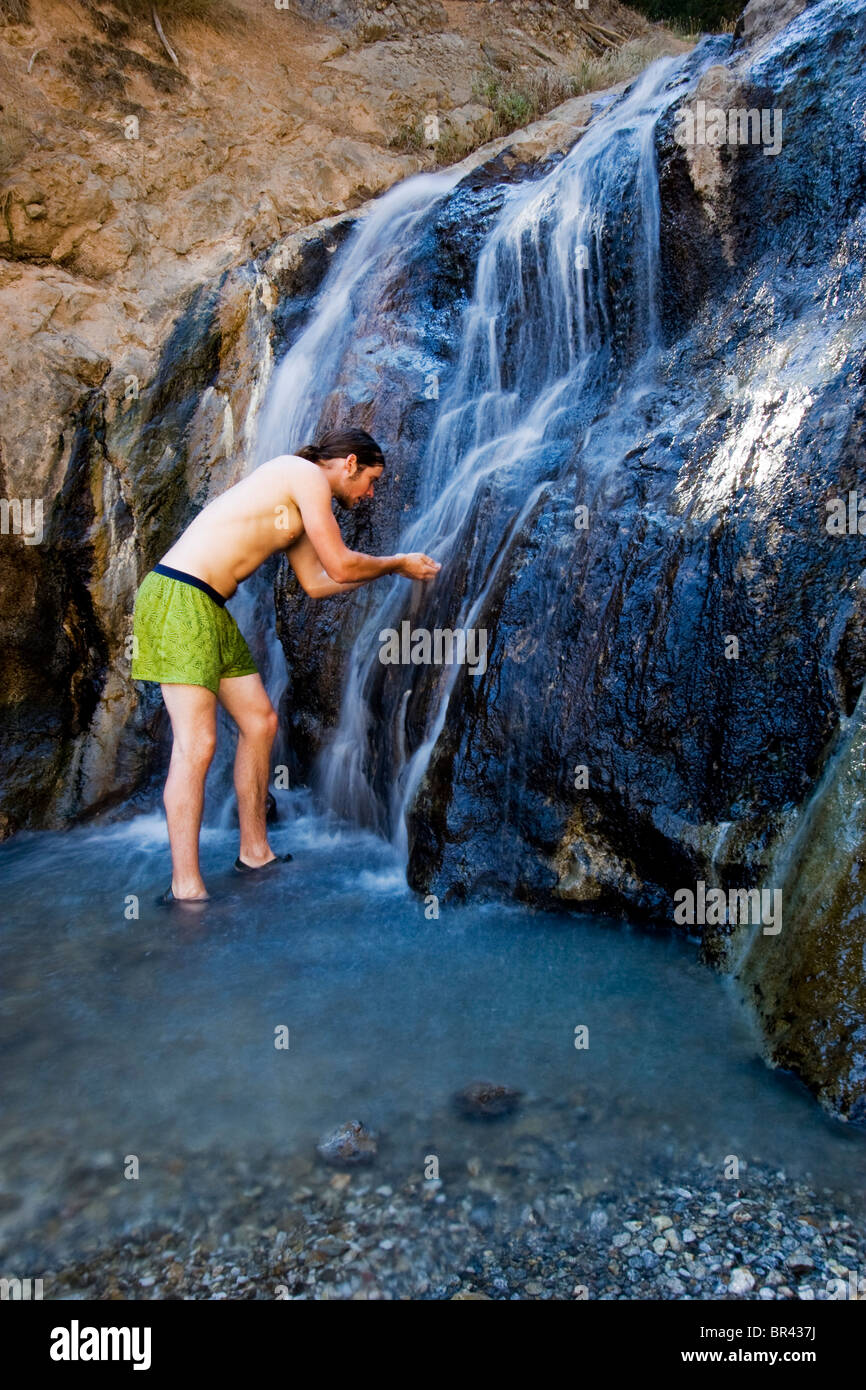 A young man cups water with his hands while enjoying a hot spring of a ...