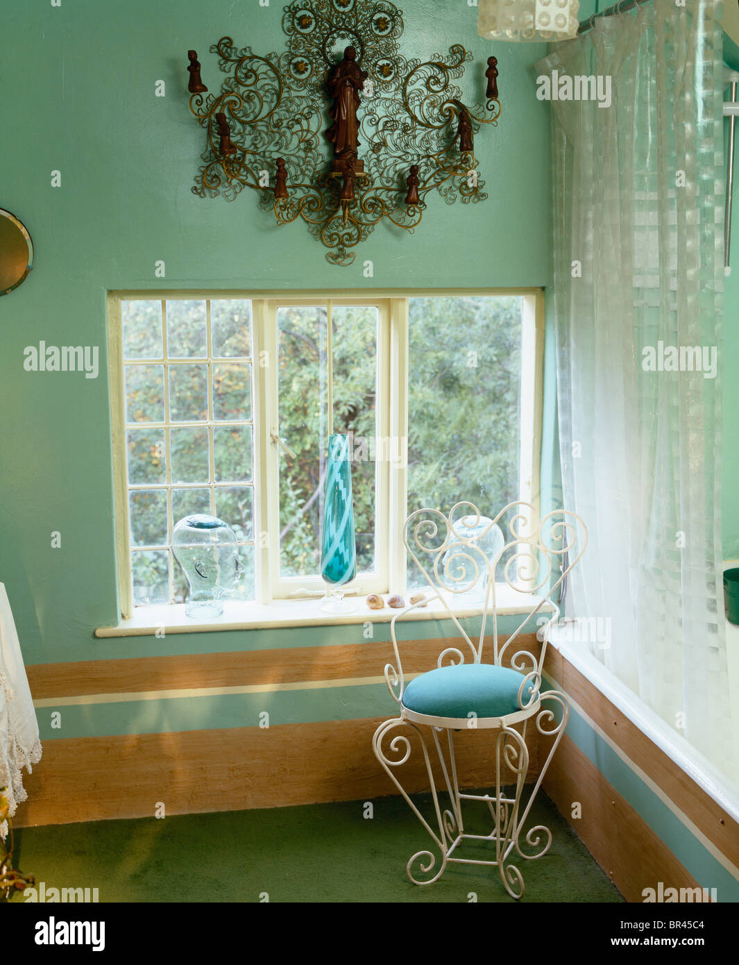 Ornate metal wall sconce above window of pale green bathroom with white ...