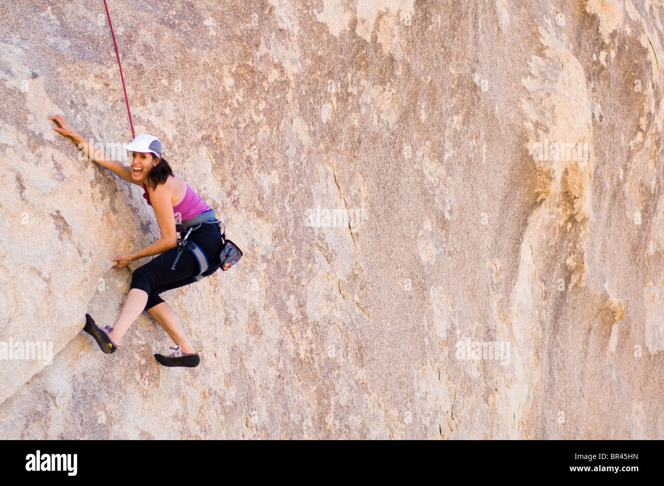A climber smiles and laughs while climbing a rock route in Joshua Tree ...