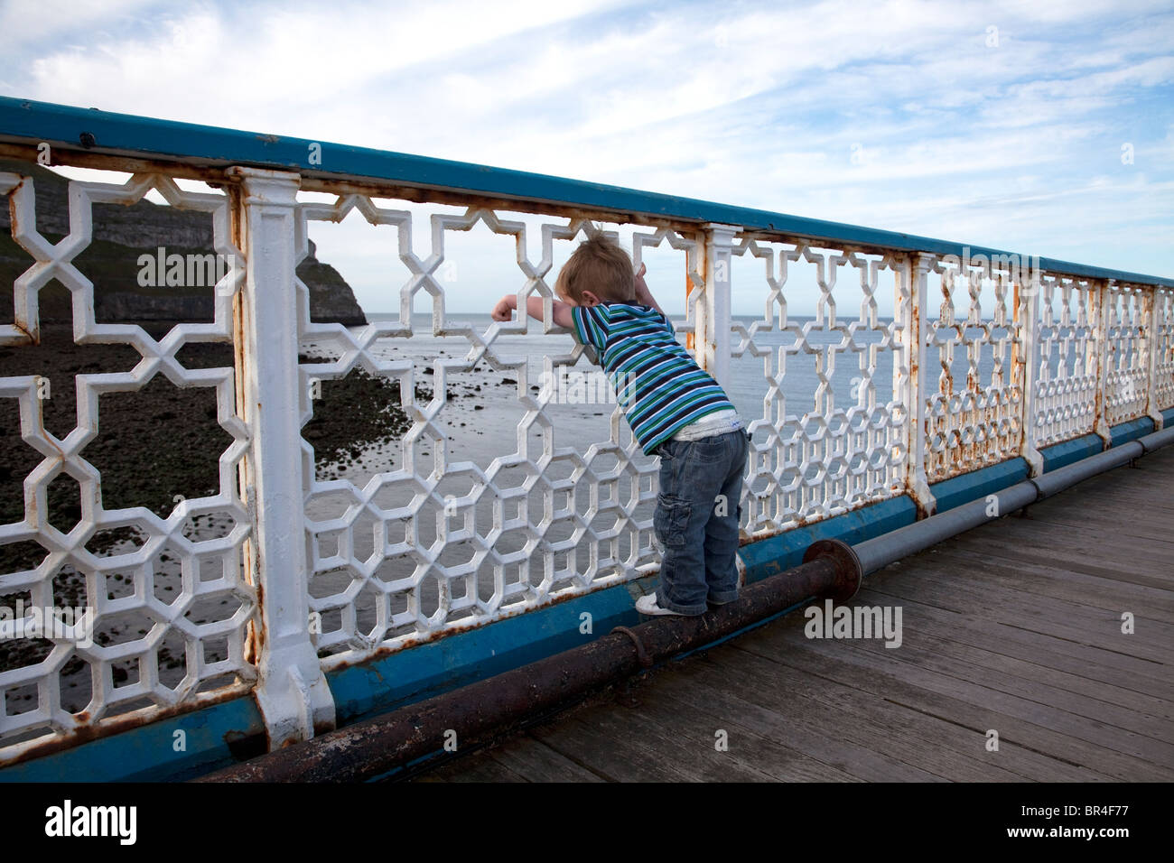 Young boy looking through railings on the pier at Llandudno North Wales ...