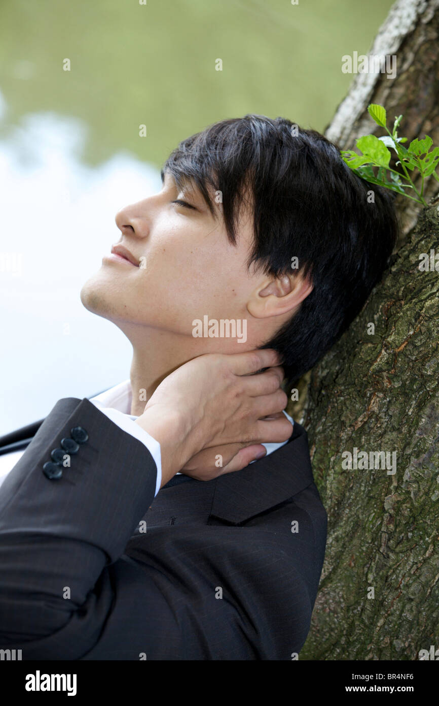 Young businessman leaning against tree trunk, profile Stock Photo - Alamy