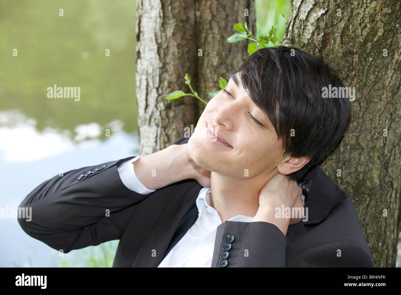 Young businessman leaning against tree trunk Stock Photo - Alamy