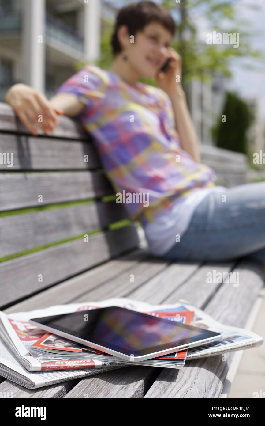 Young woman cell phone, iPad, newspapers and magazine on a bench Stock ...