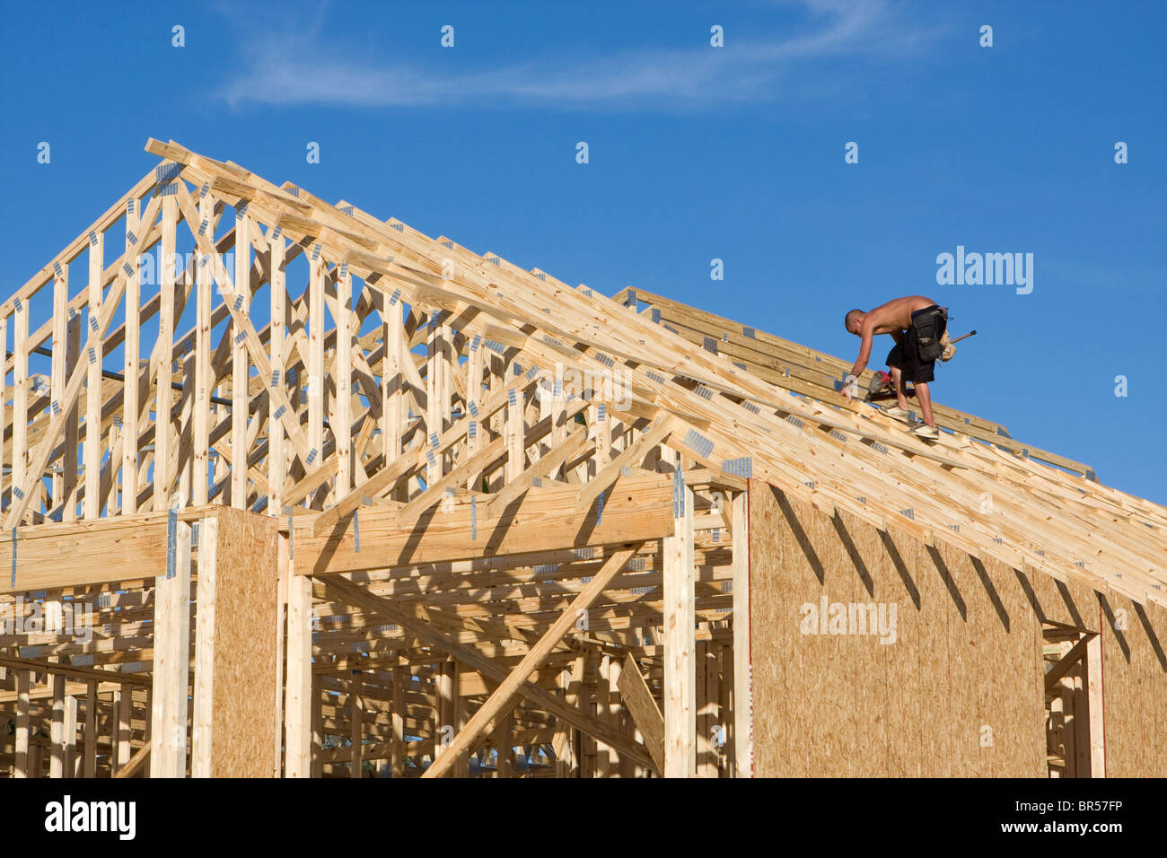 Carpenter uses a pneumatic nail gun to add braces to a truss roof on a ...