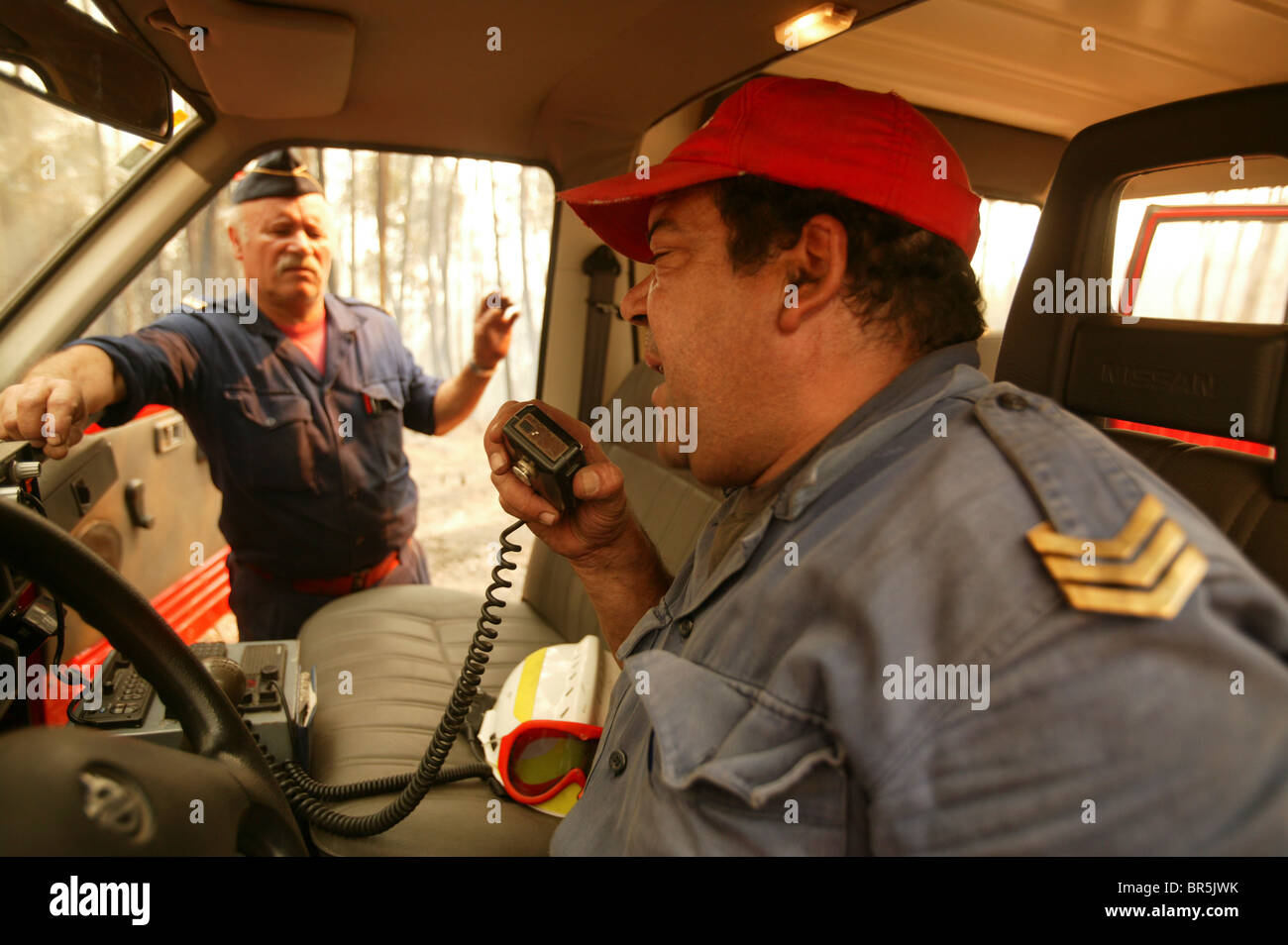 Two firemen on a firetruck talk on the radio to come up with a strategy ...