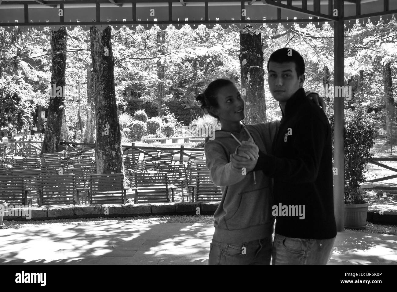 Couple of boy and girl dancing under a gazebo, chairs and trees ...
