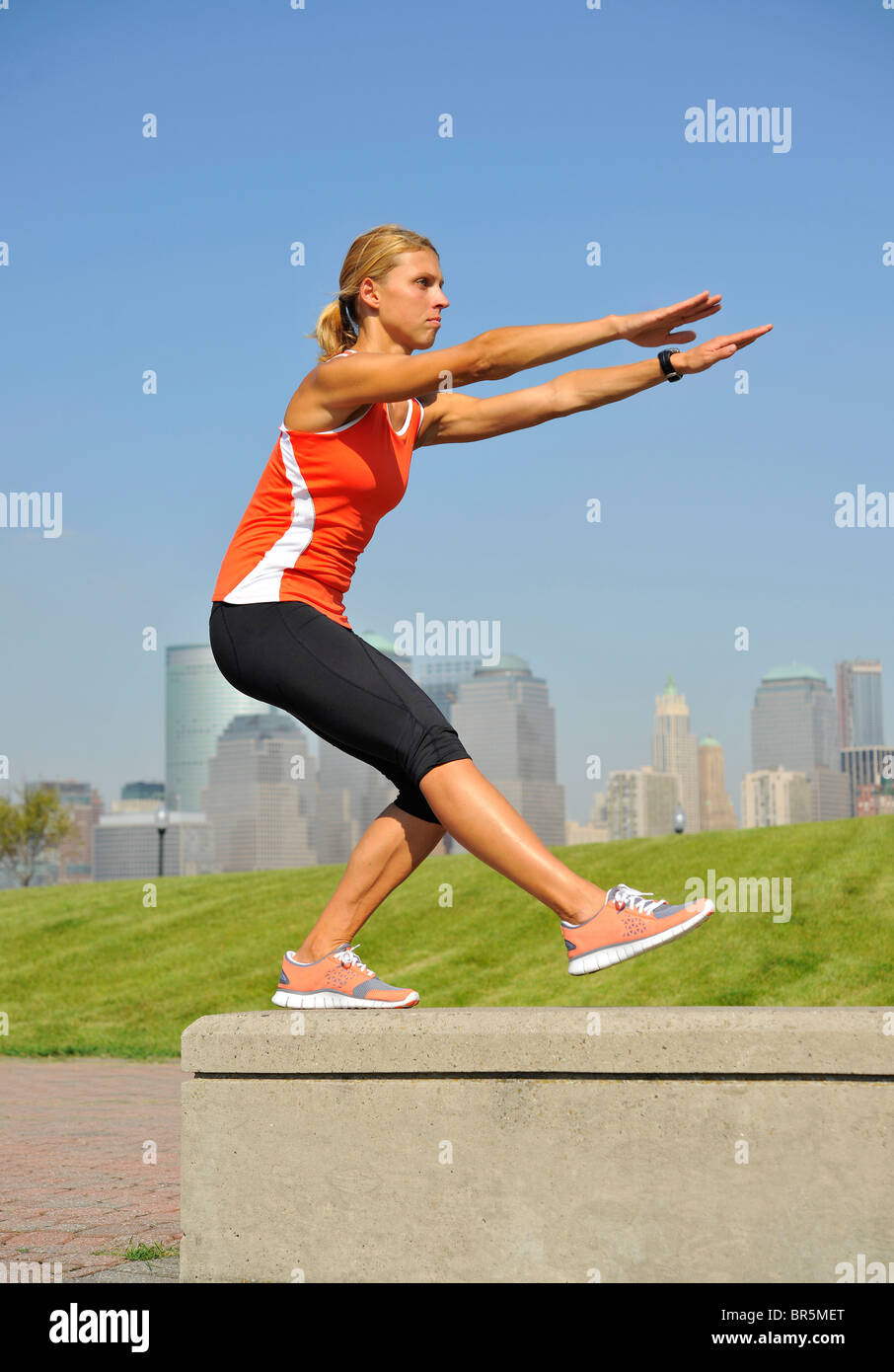 Athletic blond woman doing stretching exercise at sunny park in front ...