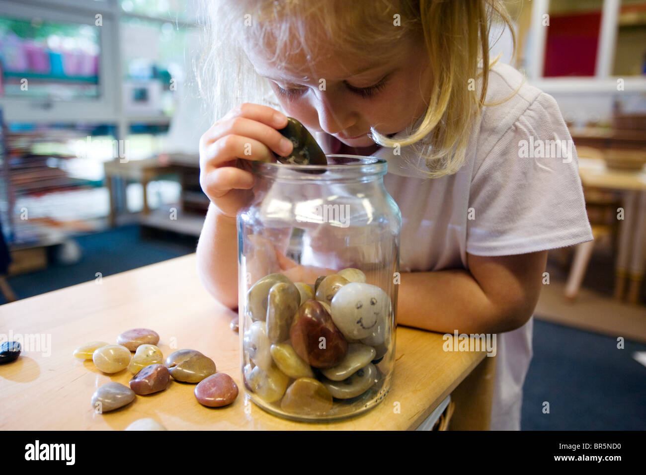 A girl in a UK nursery school collecting pebbles in a glass jar Stock ...