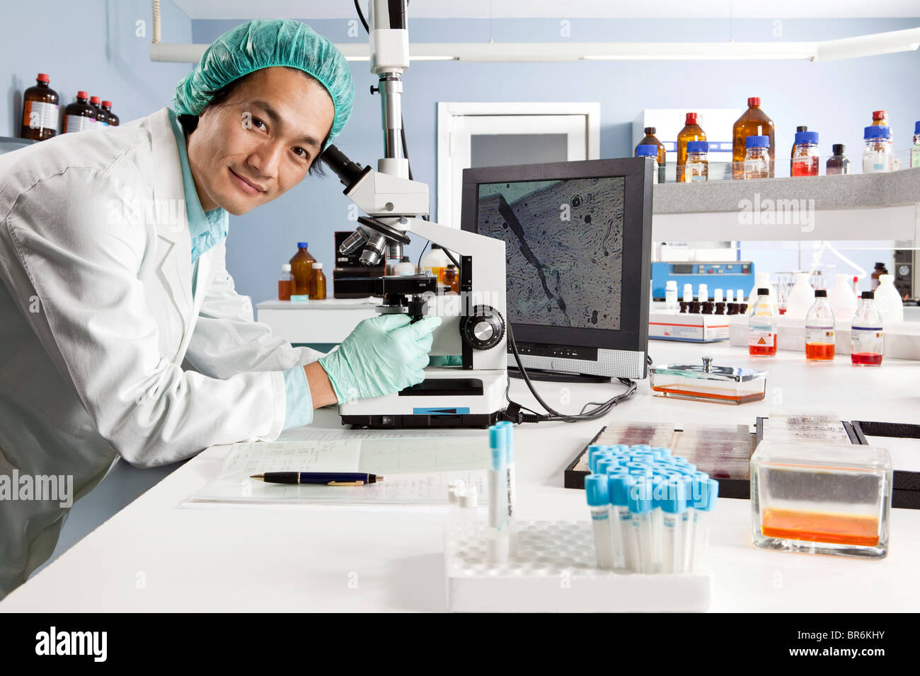 A lab technician using a microscope, looking at camera Stock Photo - Alamy
