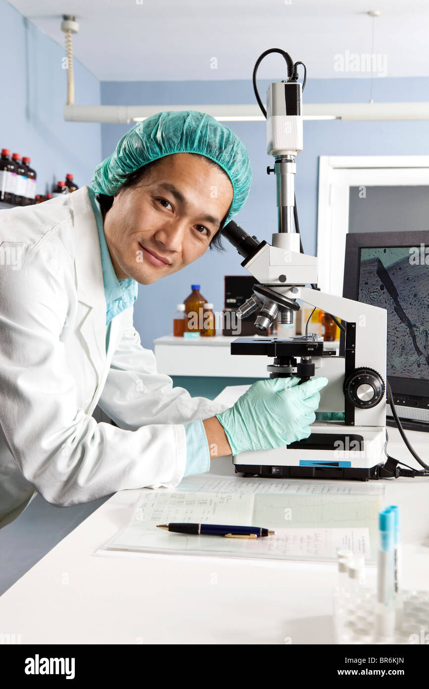 A lab technician using a microscope, looking at camera Stock Photo - Alamy