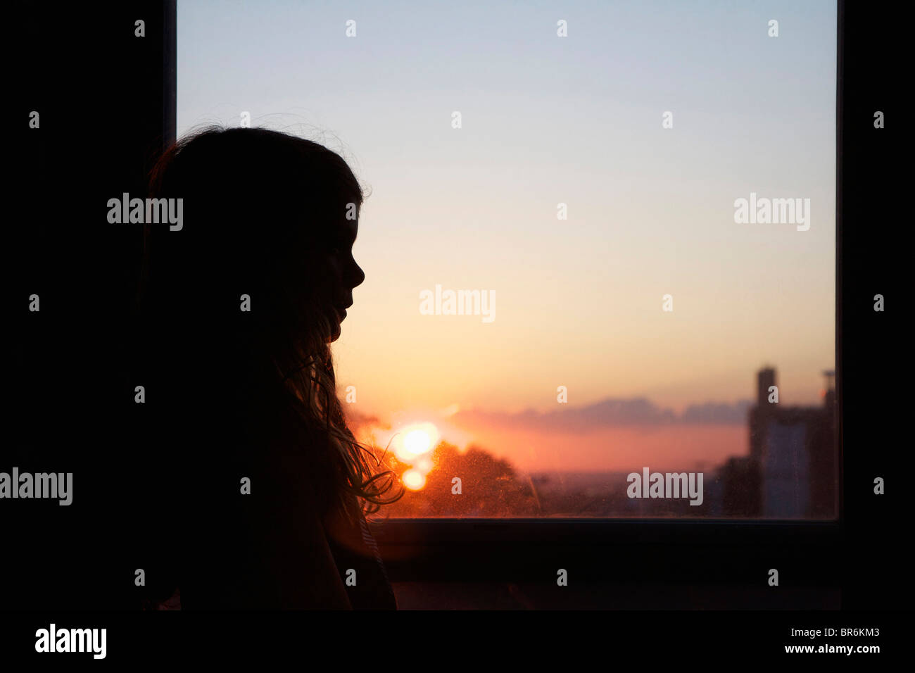 A girl by a window at sunset Stock Photo - Alamy