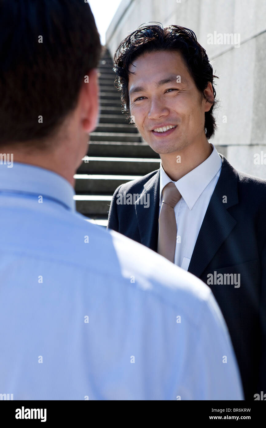 A businessman talking to a colleague, outdoors, over the shoulder view ...