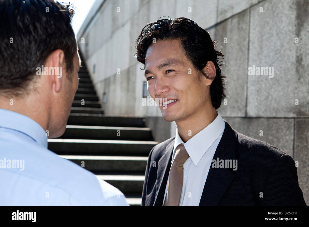 A businessman listening to a colleague, outdoors, over the shoulder ...