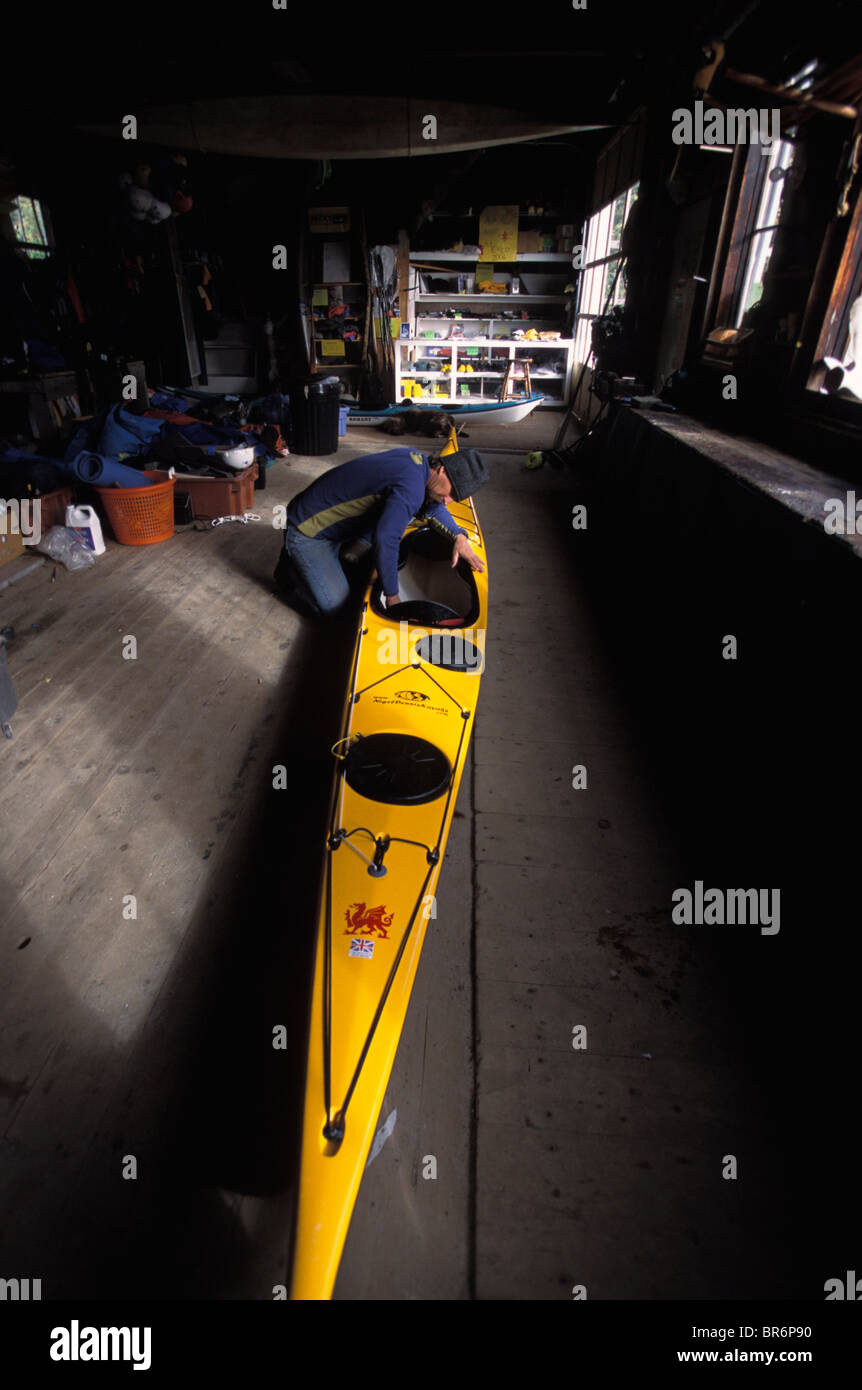A man in a boathouse prepares his sea kayak for a day of sea kayaking ...