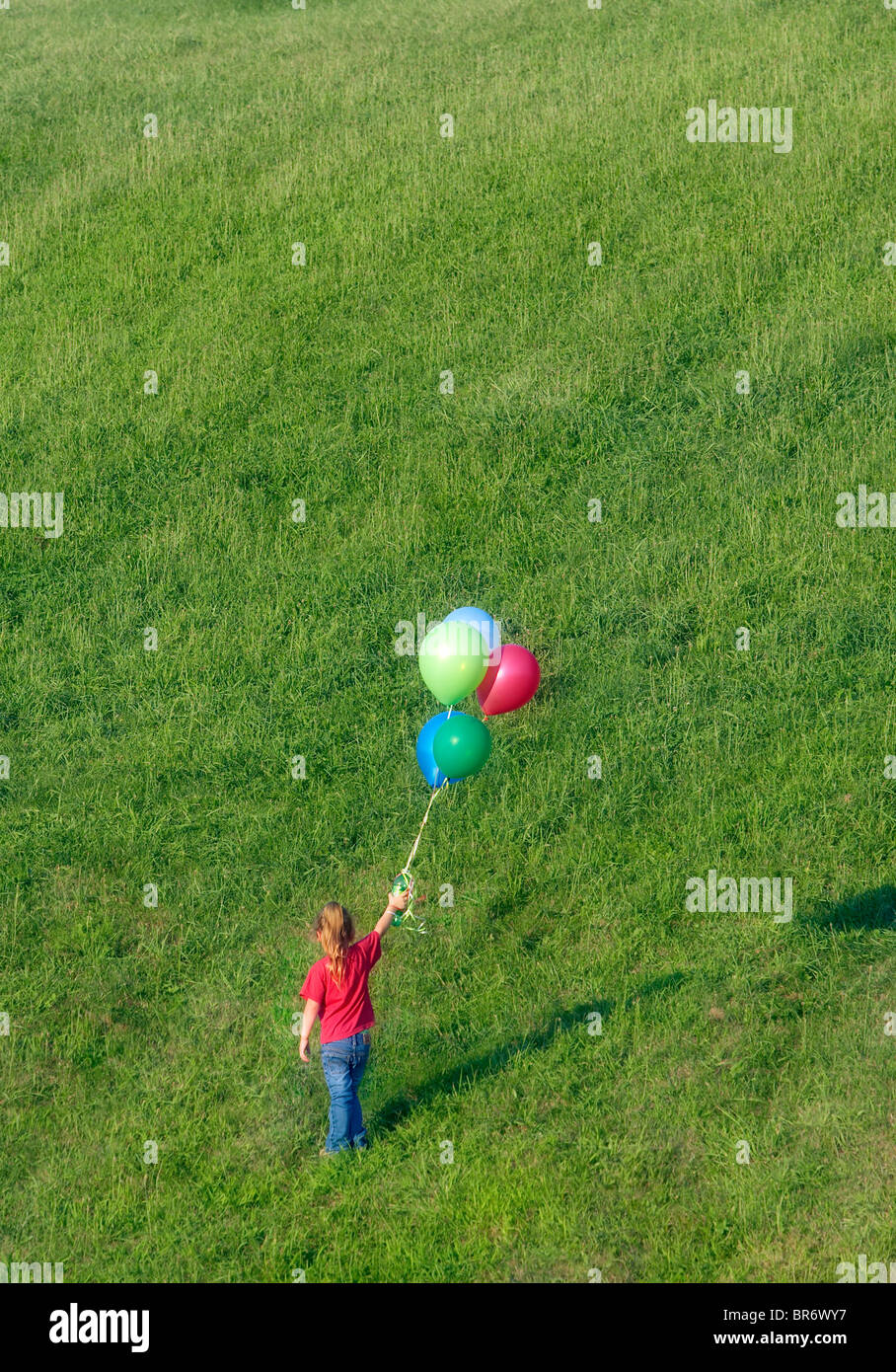A young girl holding balloons stands alone in a field Durham ...