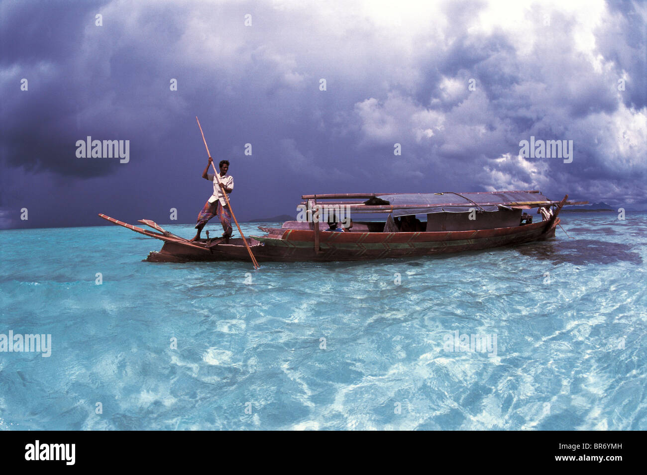 Bajau fisherman in traditional Lepa boat with rain clouds behind, Pulau ...