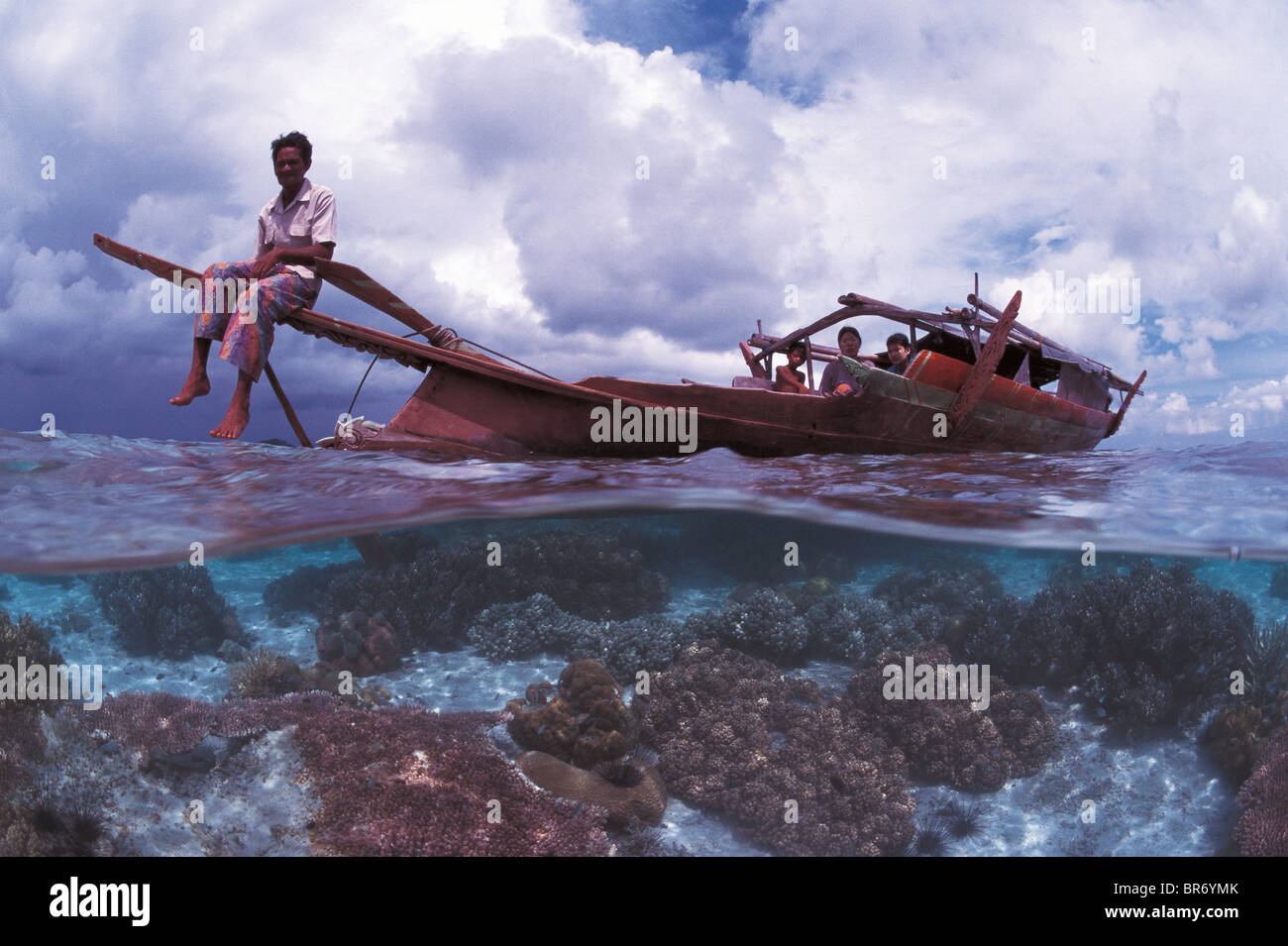 Bajau fisherman on traditional Lepa boat in shallow water over coral ...