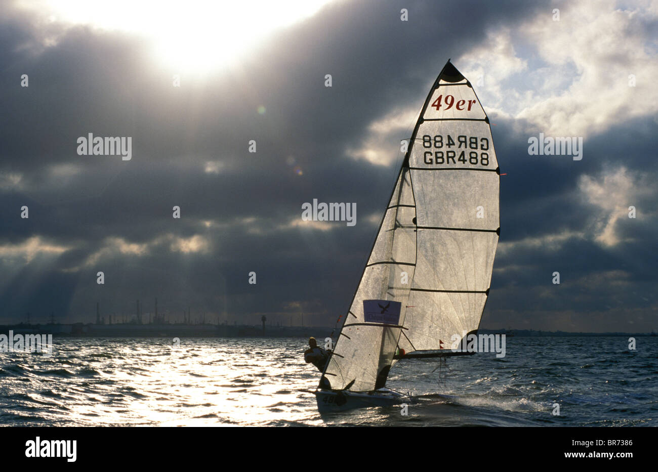 Sun reflects through the transparent sails of a 49er on a thundery day ...
