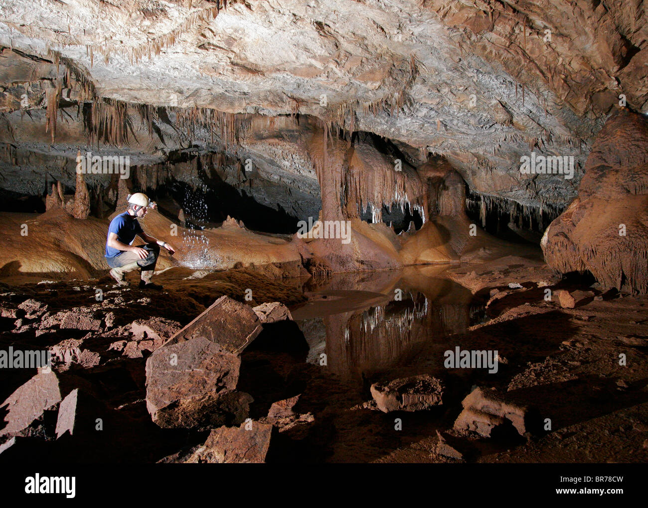 A cave explorer crouching by a pool of water in a cave in Mulu National ...