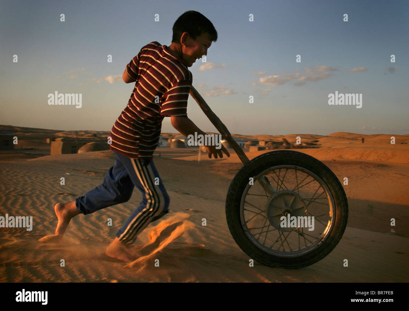 Turkmen boy pushing a wheel in the desert Stock Photo - Alamy