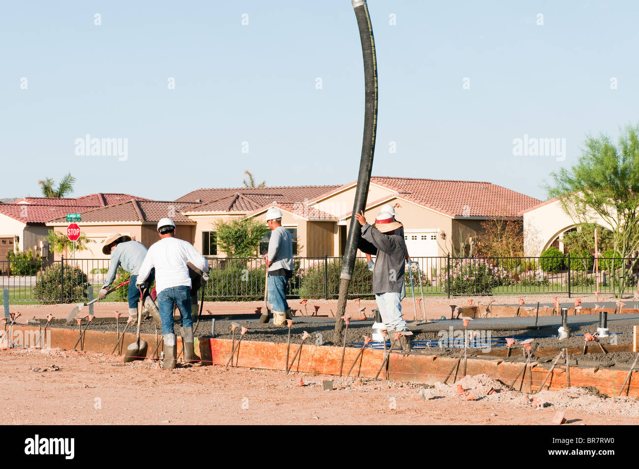 A crew of workers pour a concrete slab for a new house under ...