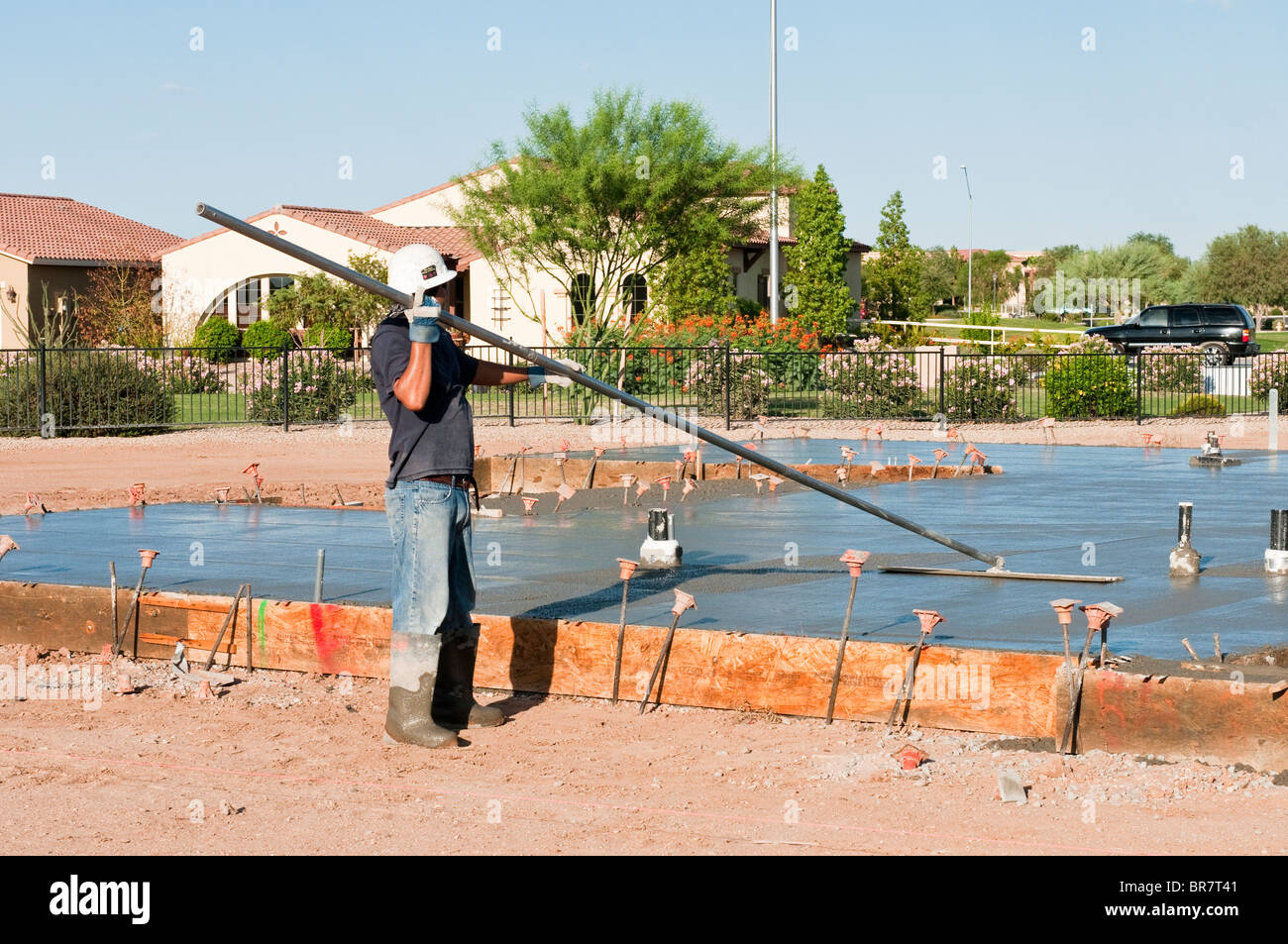 A construction worker finishes a newly poured concrete slab with a ...