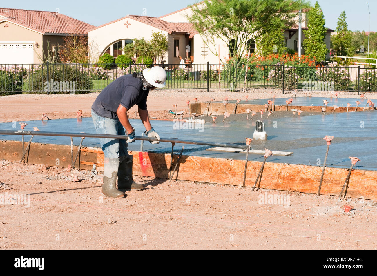 A construction worker finishes a newly poured concrete slab with a ...