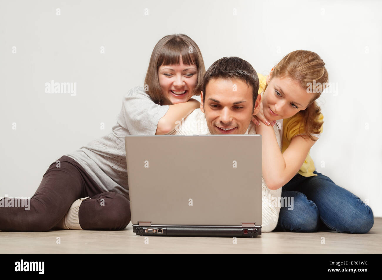 Group of three happy people lying on the floor with laptop computer ...