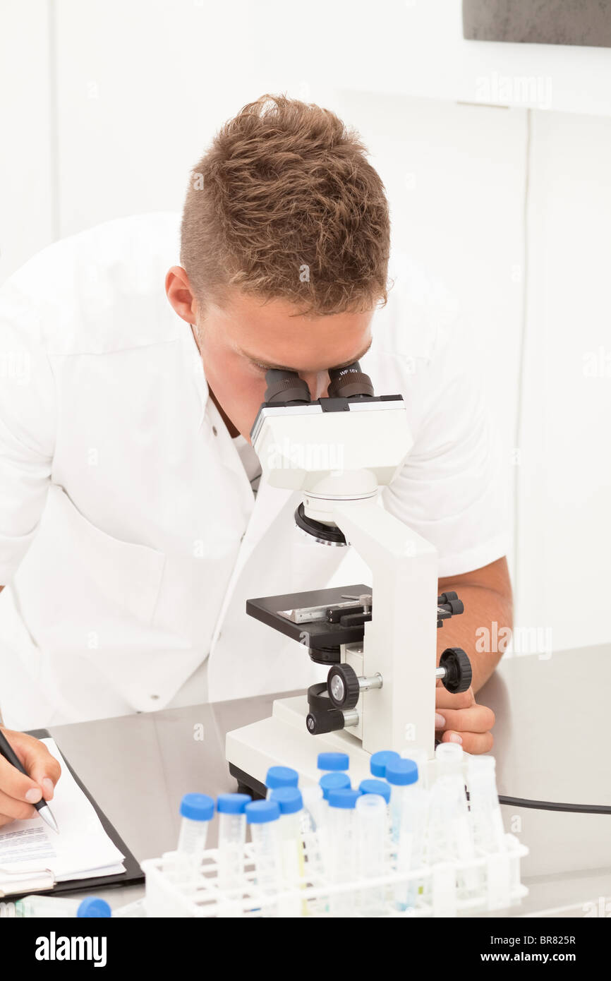 Laboratory work: young researcher looks in microscope and takes notes ...