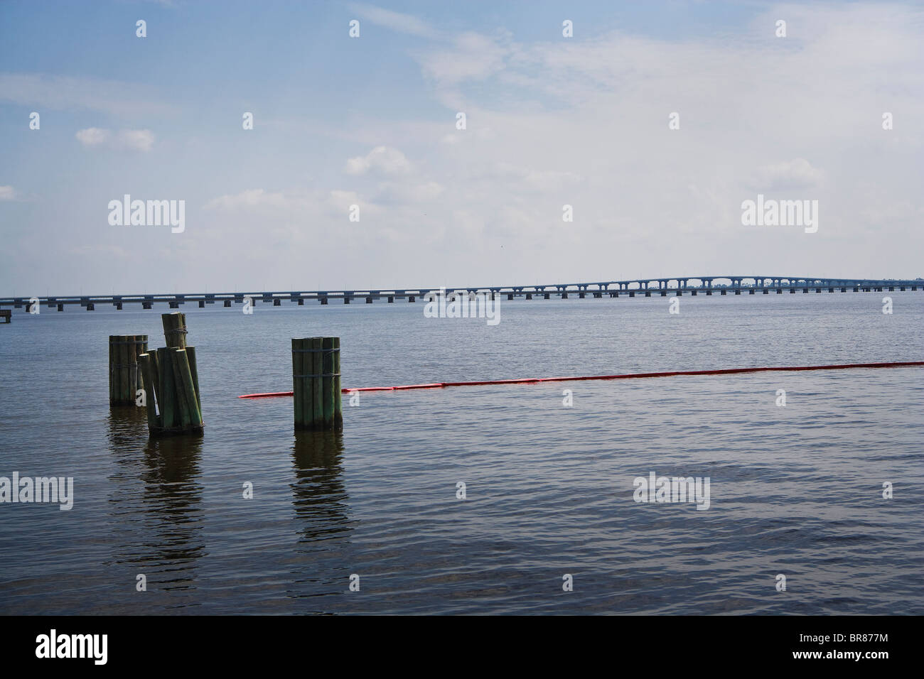 Red oil boom in the water in a quiet bay with wooden pilings and a ...