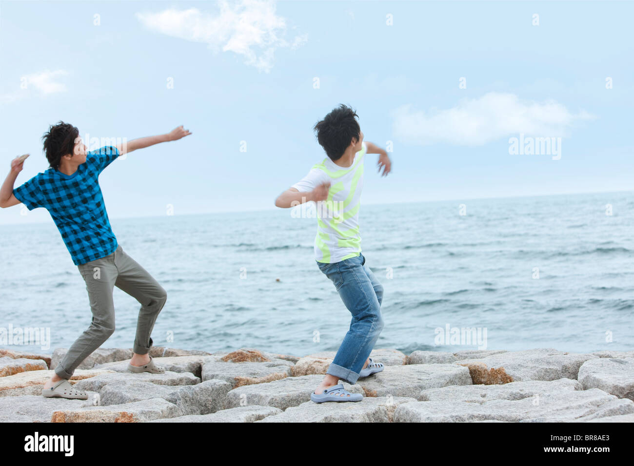Two young men throwing stones over sea, blurred motion Stock Photo - Alamy
