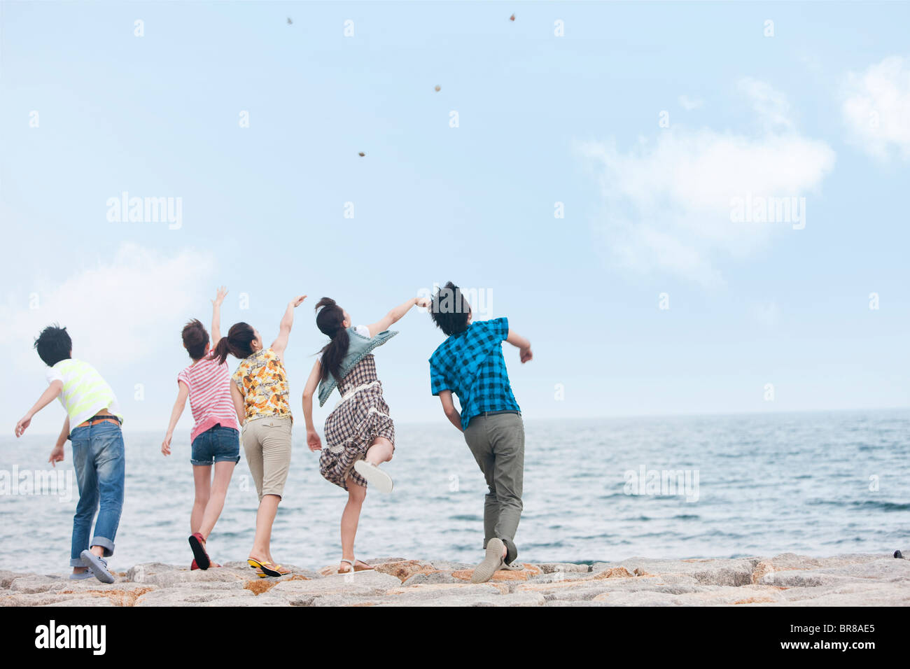 Five young people throwing stones over sea Stock Photo - Alamy