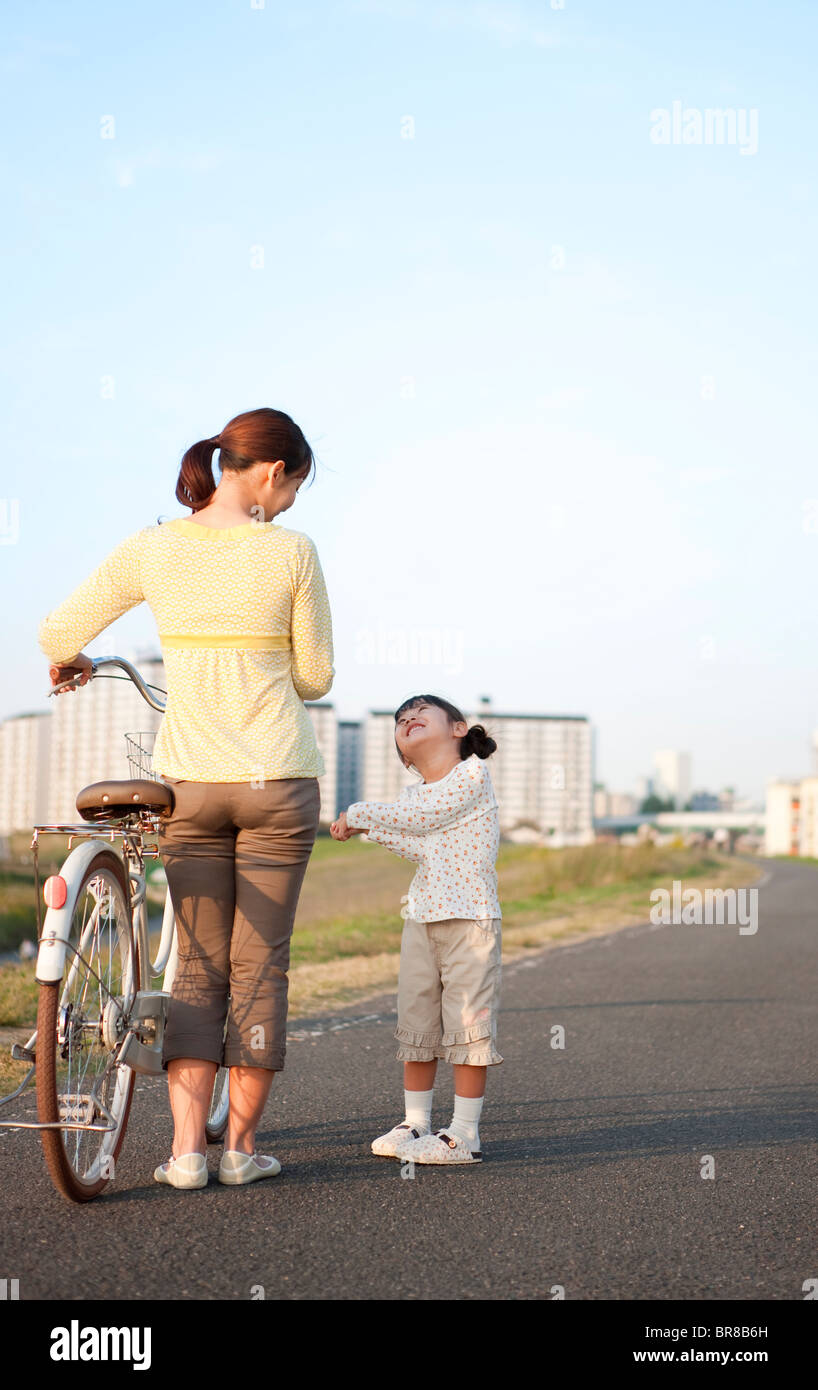 Girl with mother walking at riverbank, mother pushing bicycle, copy ...