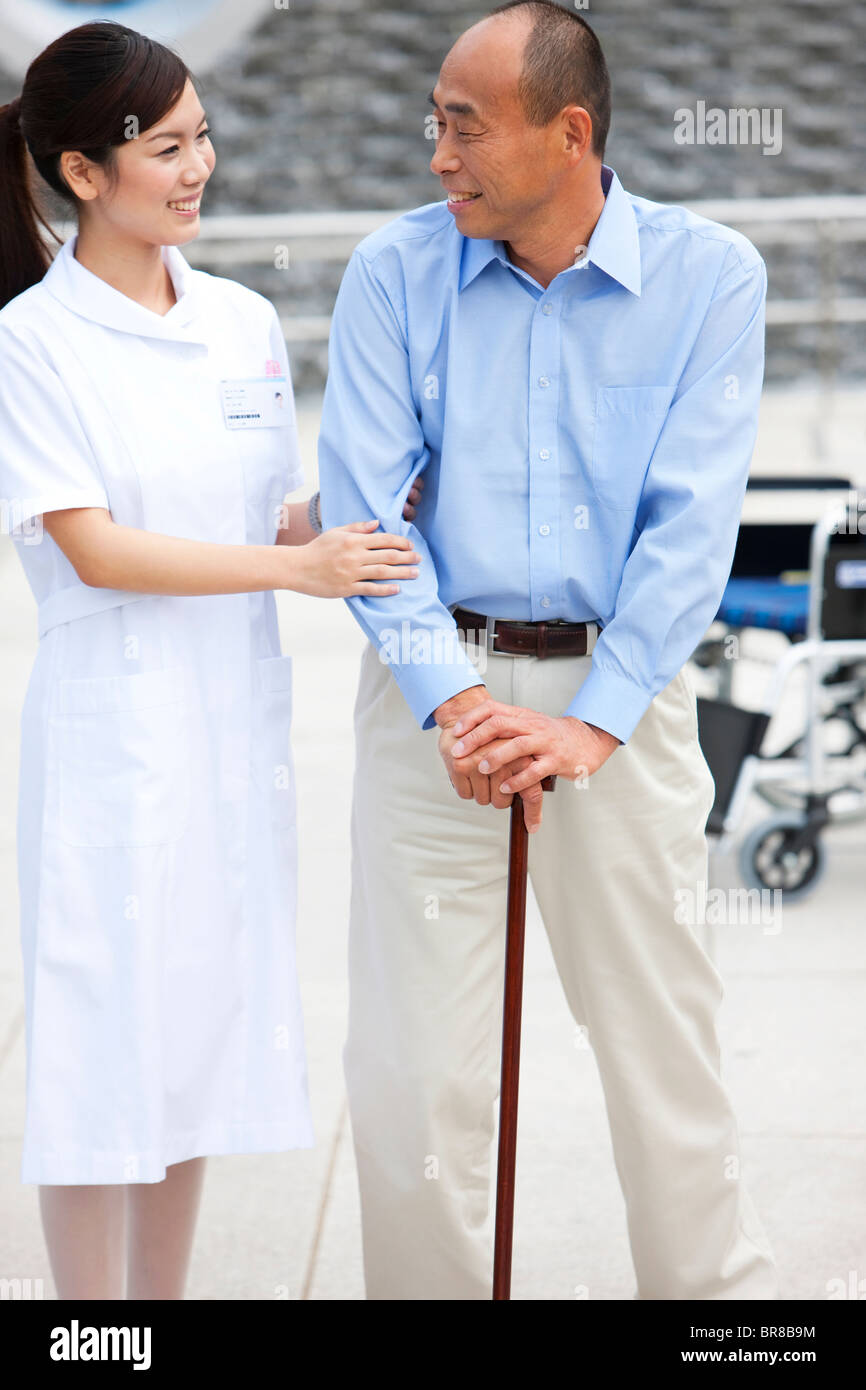 Nurse assisting man with cane Stock Photo - Alamy