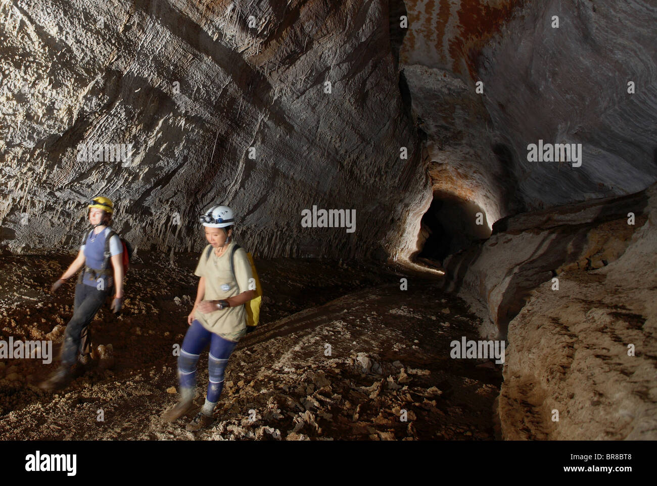 Two female cave explorers walk through a tunnel in a cave deep in the ...
