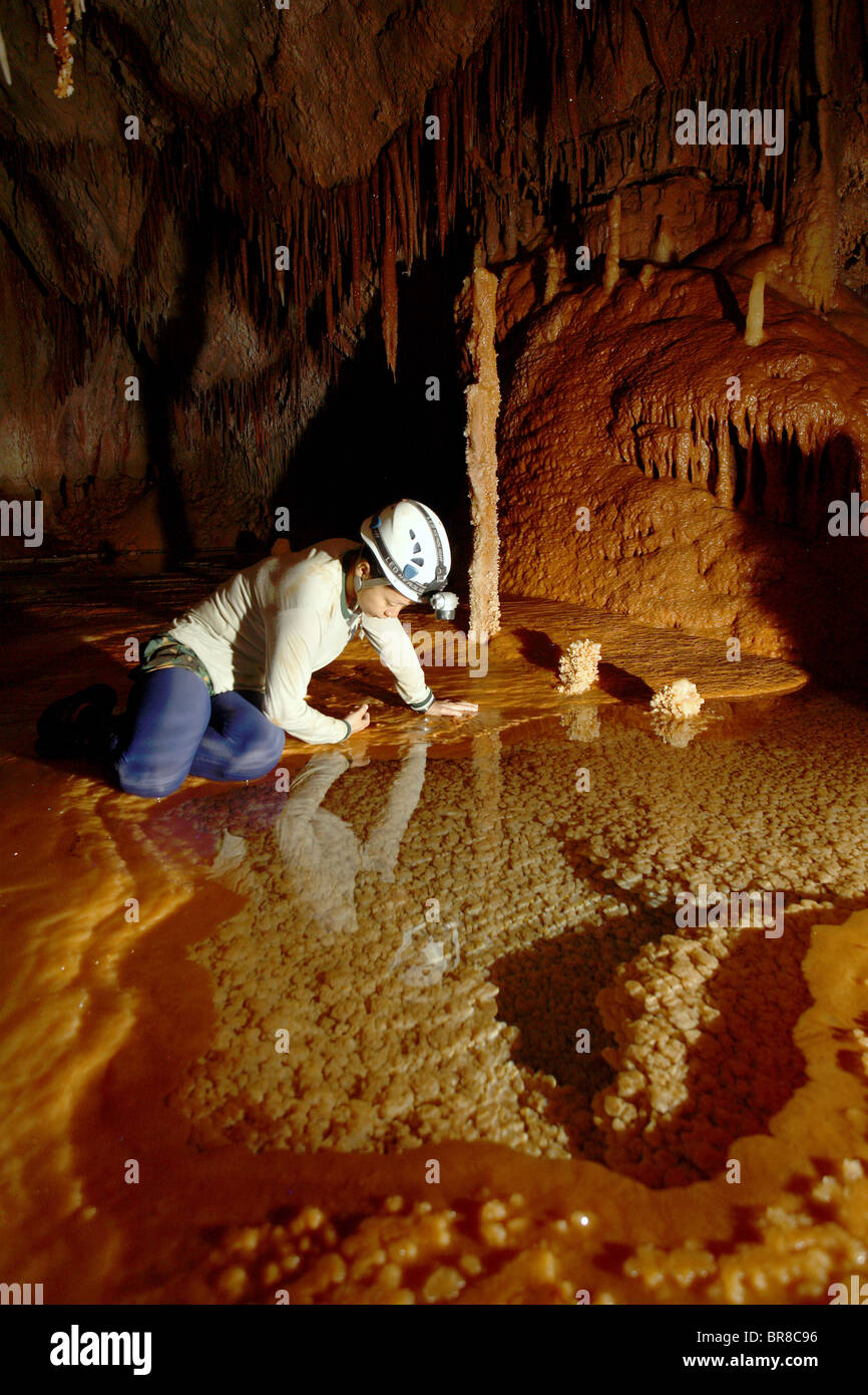 A female cave explorer looks into a crystal clear Gour Pool surrounded ...