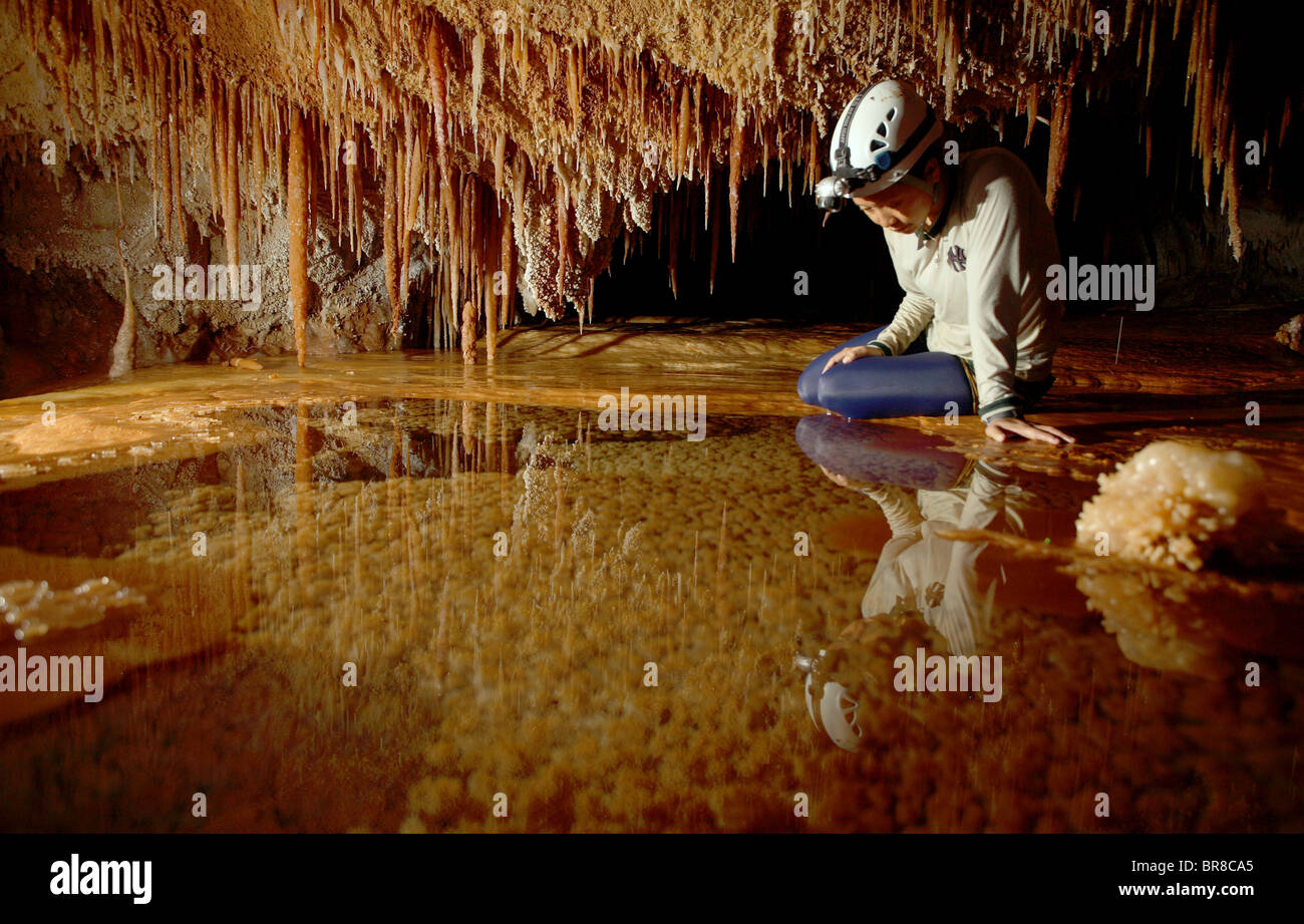 A female cave explorer looks into a crystal clear Gour Pool surrounded ...