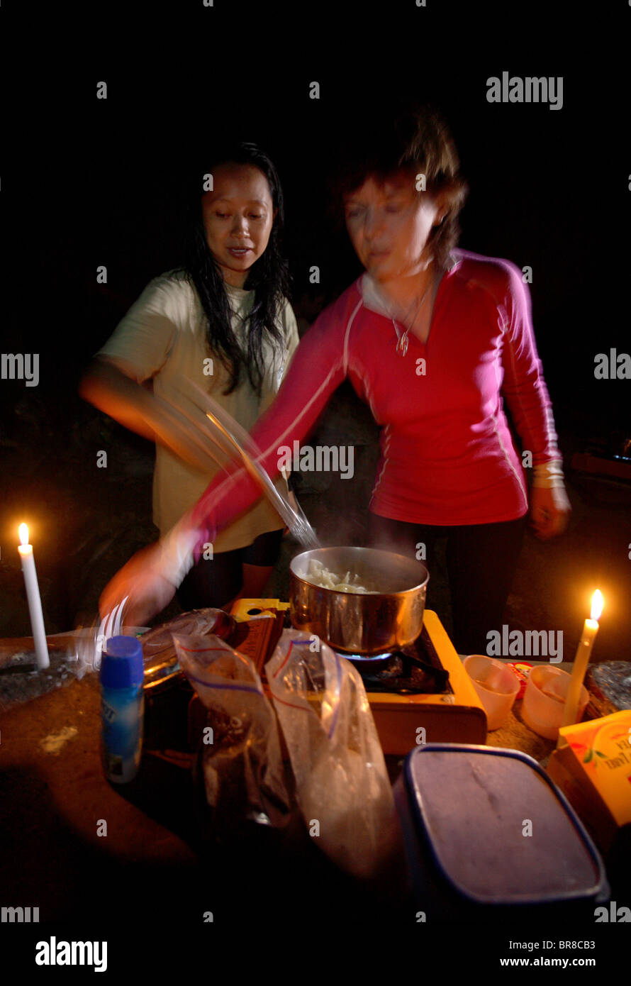 Two female cave explorers prepare an evening meal under candle light ...