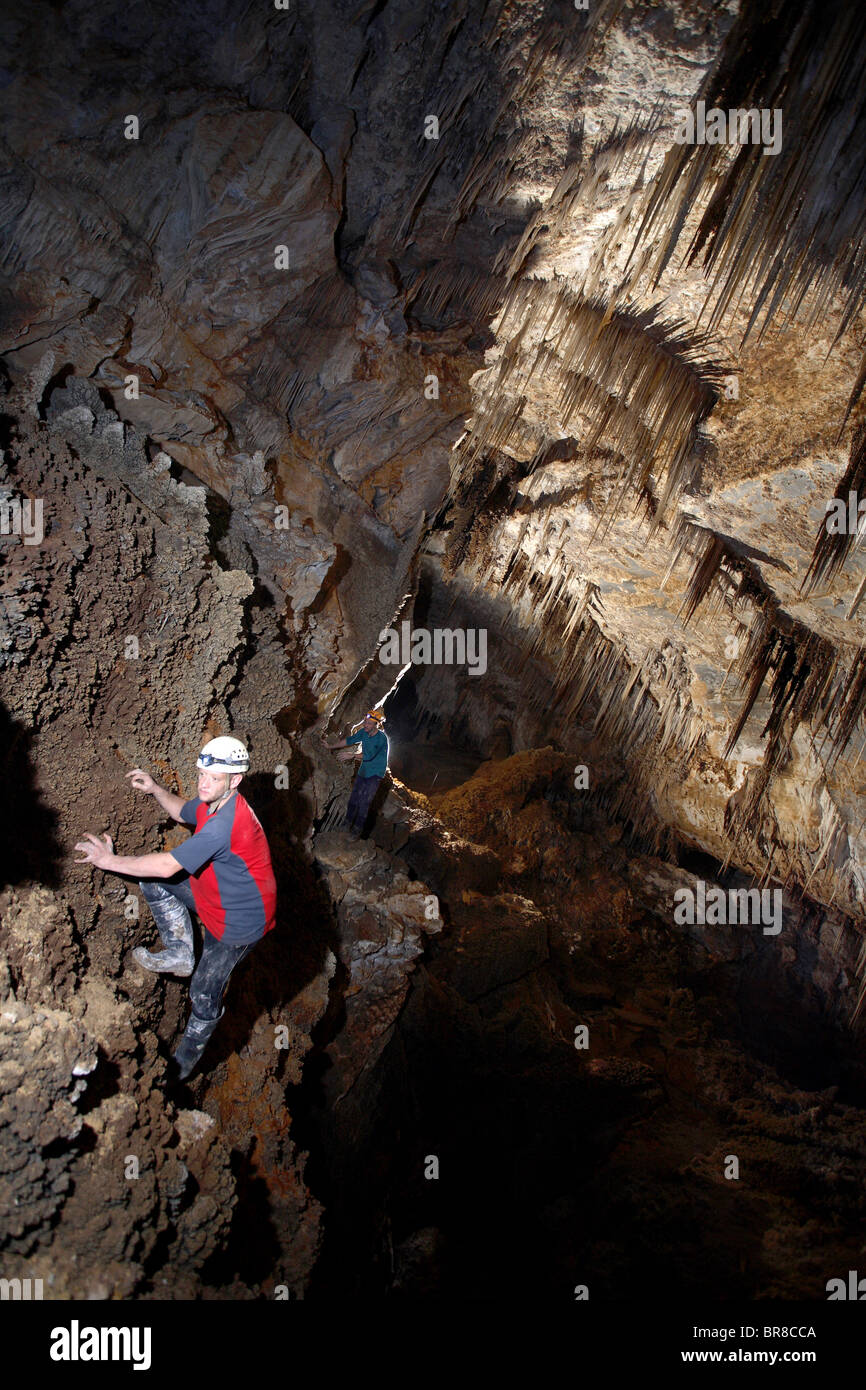 Two cave explorers traverse a section of cave on a ledge above a deep ...