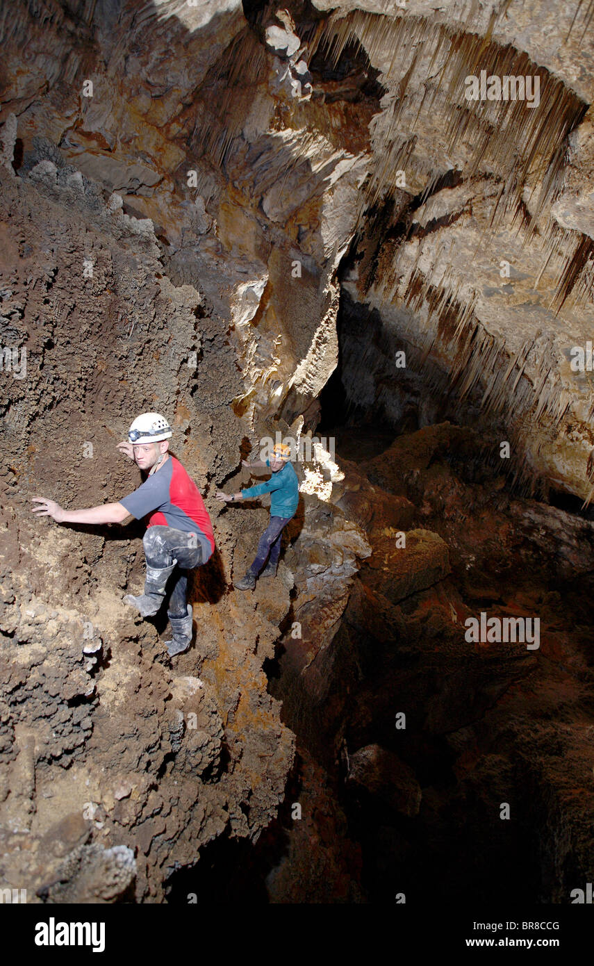 Two cave explorers traverse a section of cave on a ledge above a deep ...
