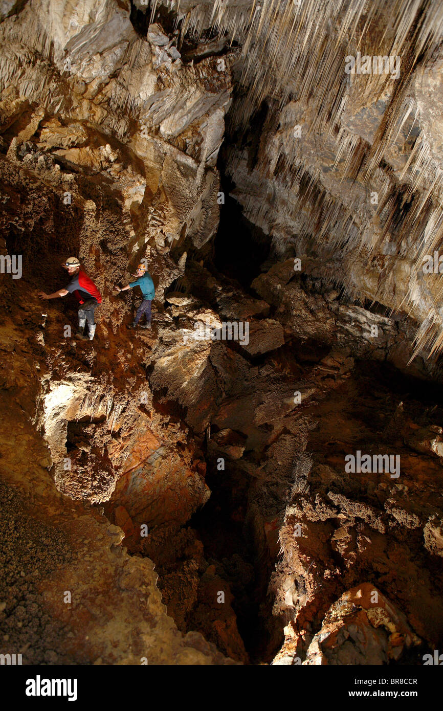 Two cave explorers traverse a section of cave on a ledge above a deep ...