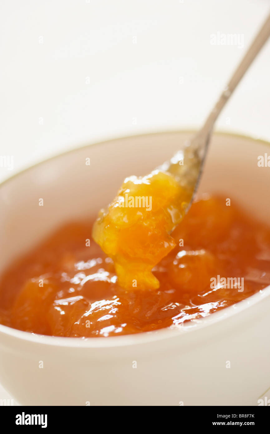 Spoon scooping apricot jam in bowl, close up, white background Stock ...
