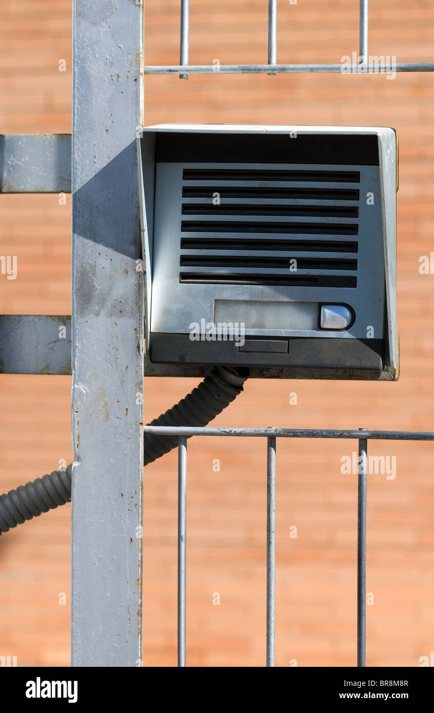 intercom box t attached to a metallic fence with a red brick building ...