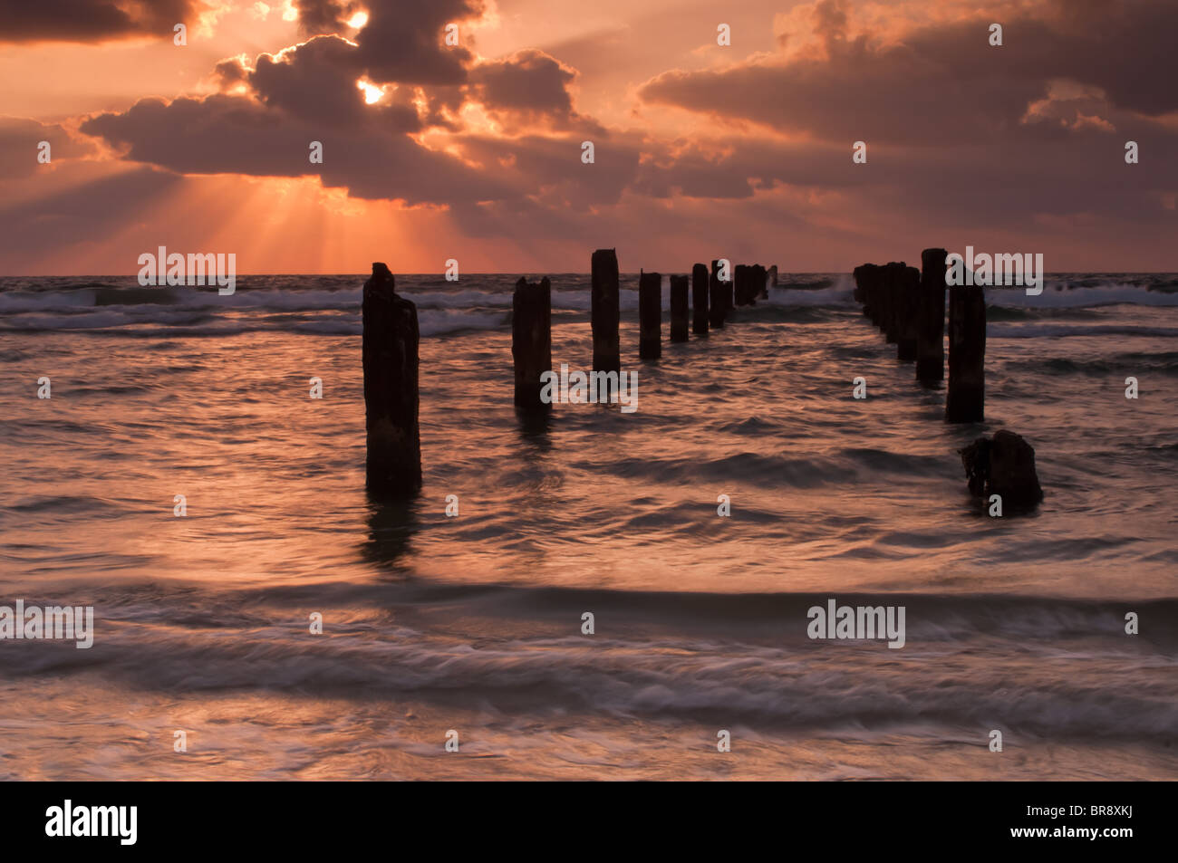Israel, Beit Yanai, Poles in the sea the remains of a wharf at sunset ...