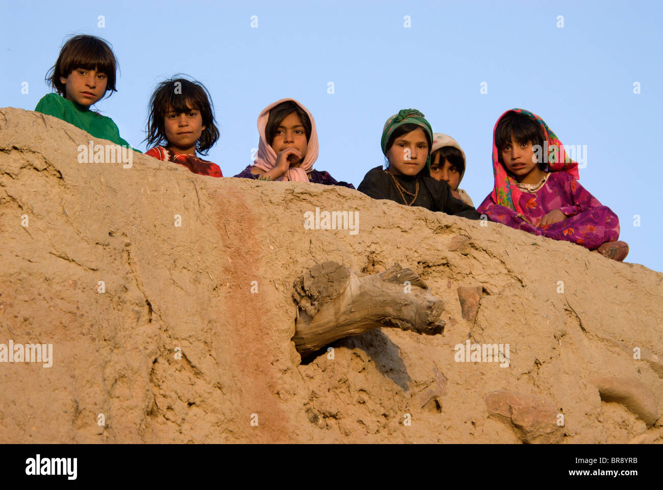 Young girls peer over the wall of a mud home in the Tajik village of ...