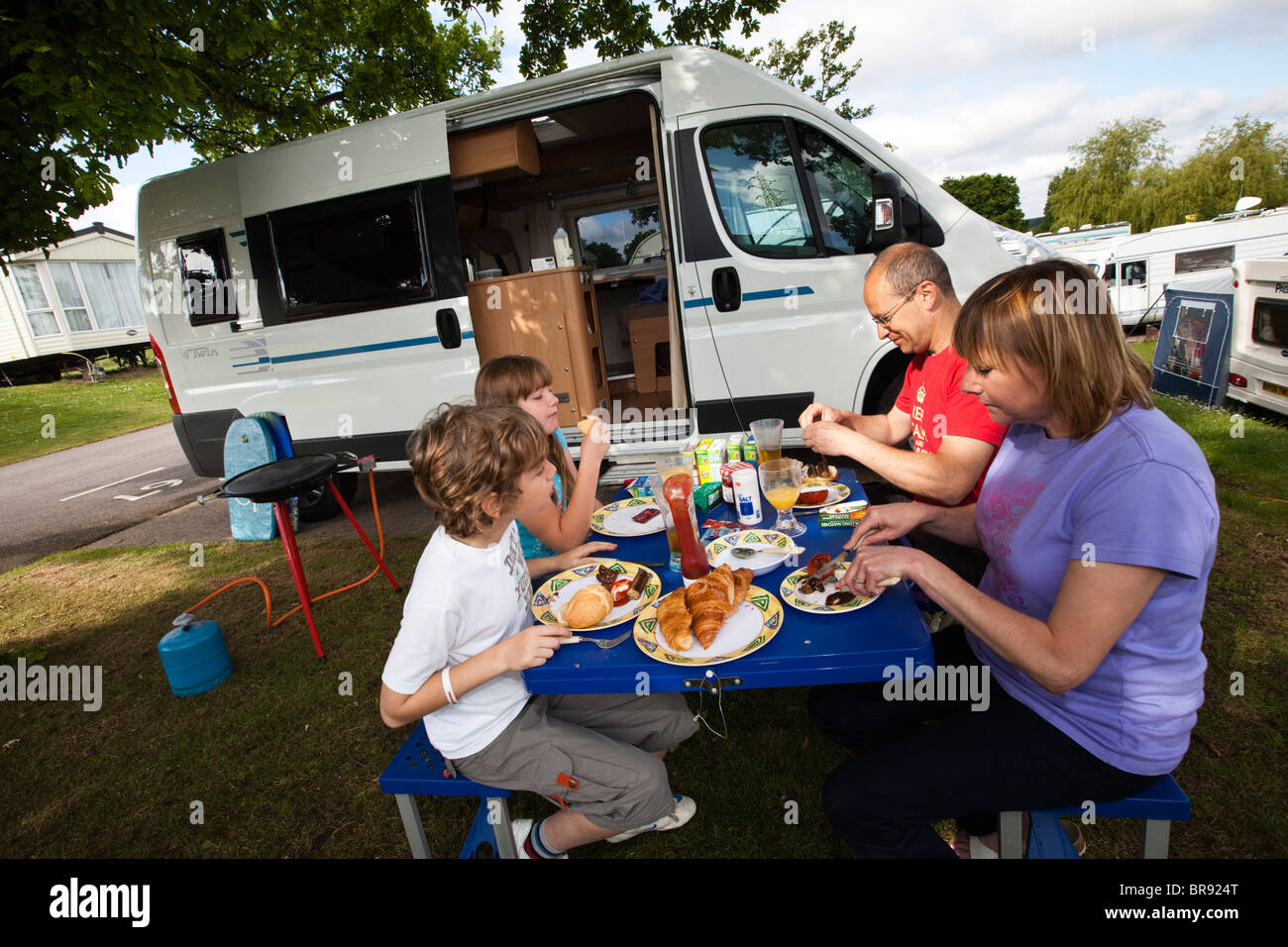 A family eating breakfast together outside there motorhome in a caravan ...